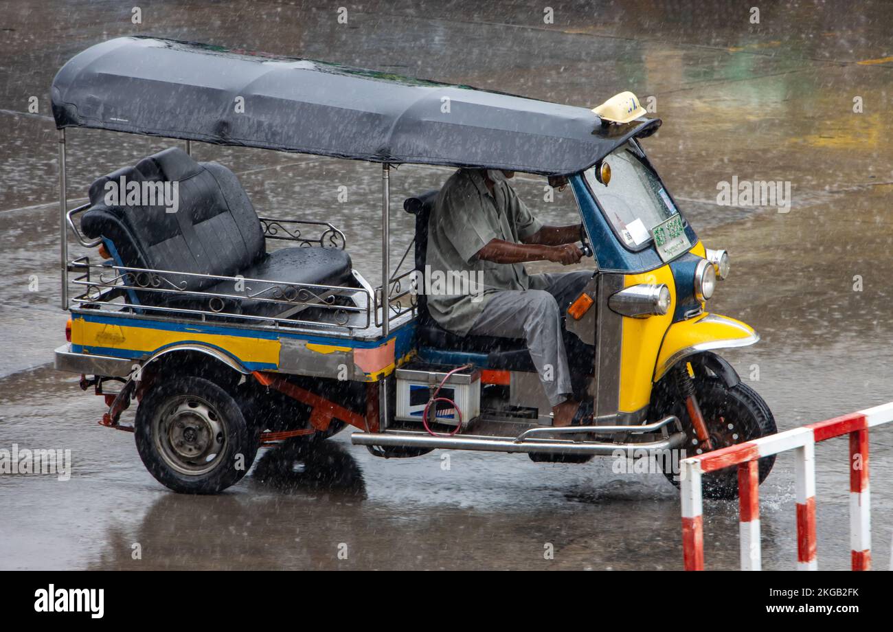 An empty Tuk Tuk motor tricycle is driving a city street in the rain ...
