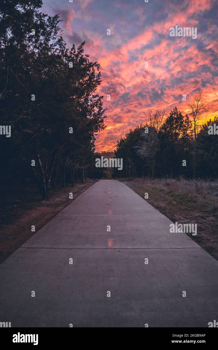 A Sunset on a sidewalk with park trees in Austin, Texas with red cloudy ...