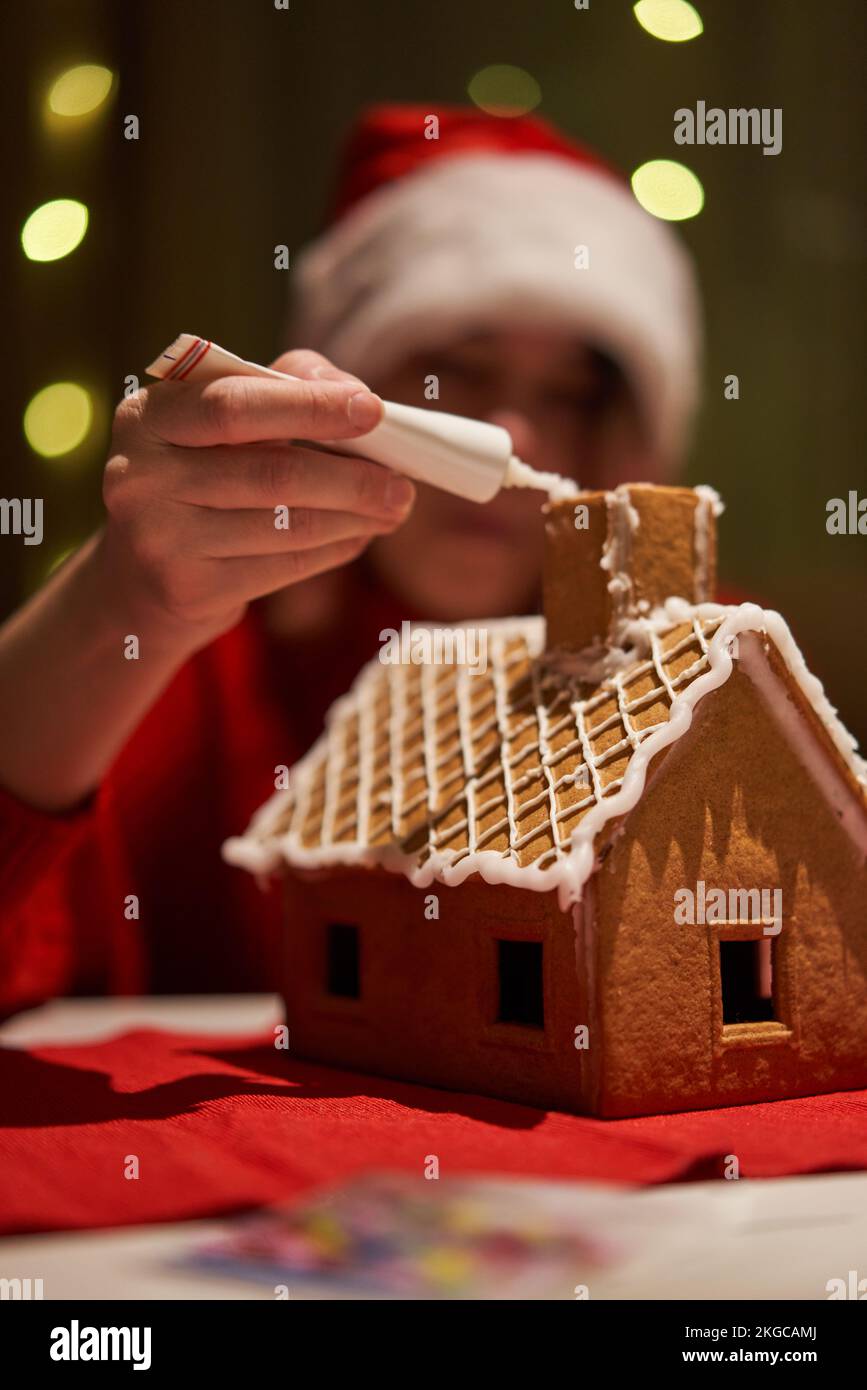 Woman in red hat building gingerbread house. Preparing to celebrate ...