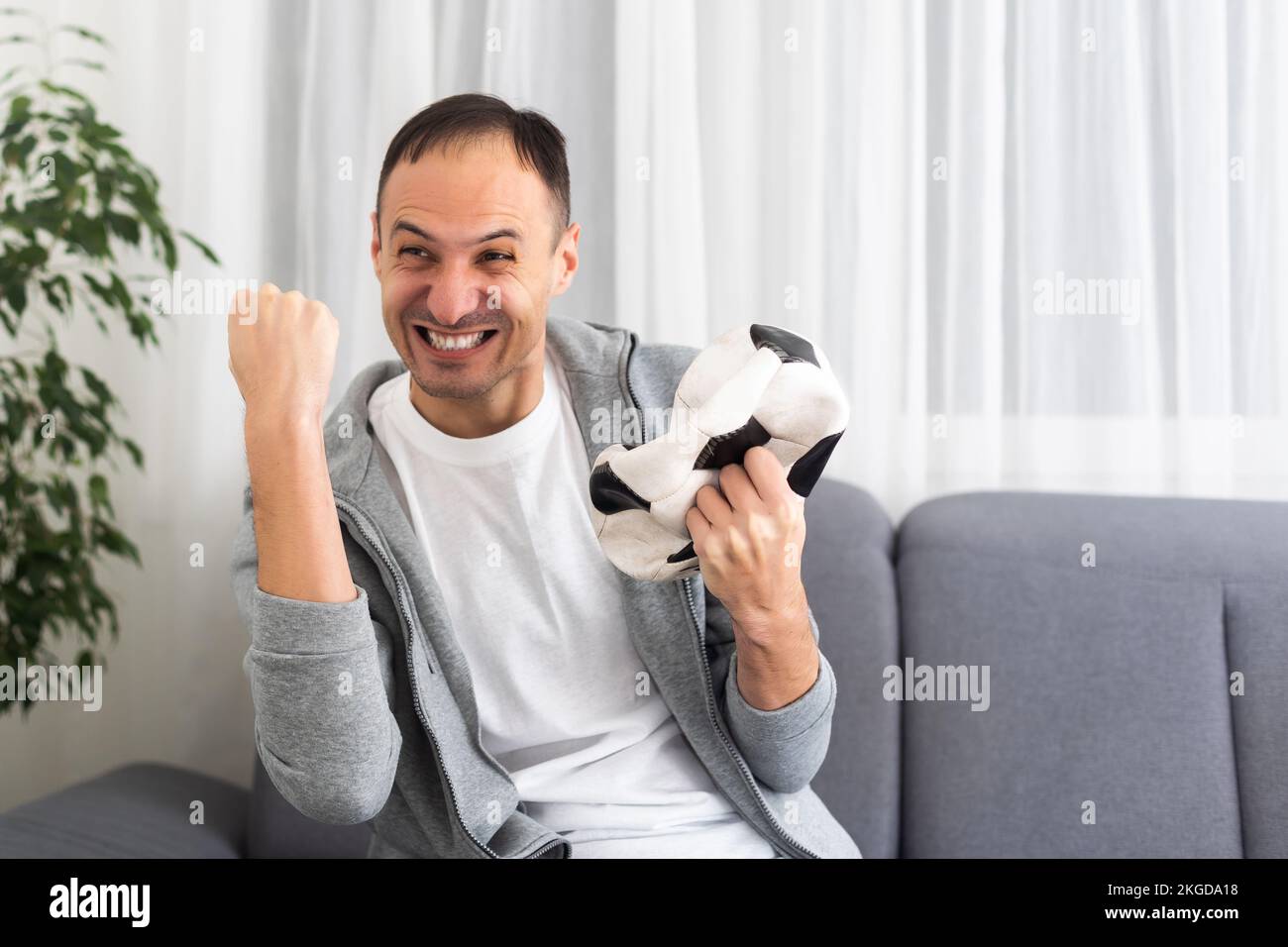 Portrait of excited young guy watching football match, raising clenched ...