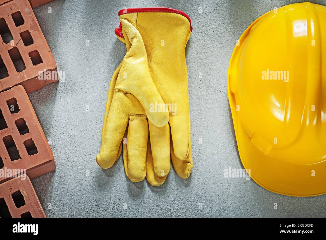Assortment of red bricks hard hat protective gloves on concrete ...