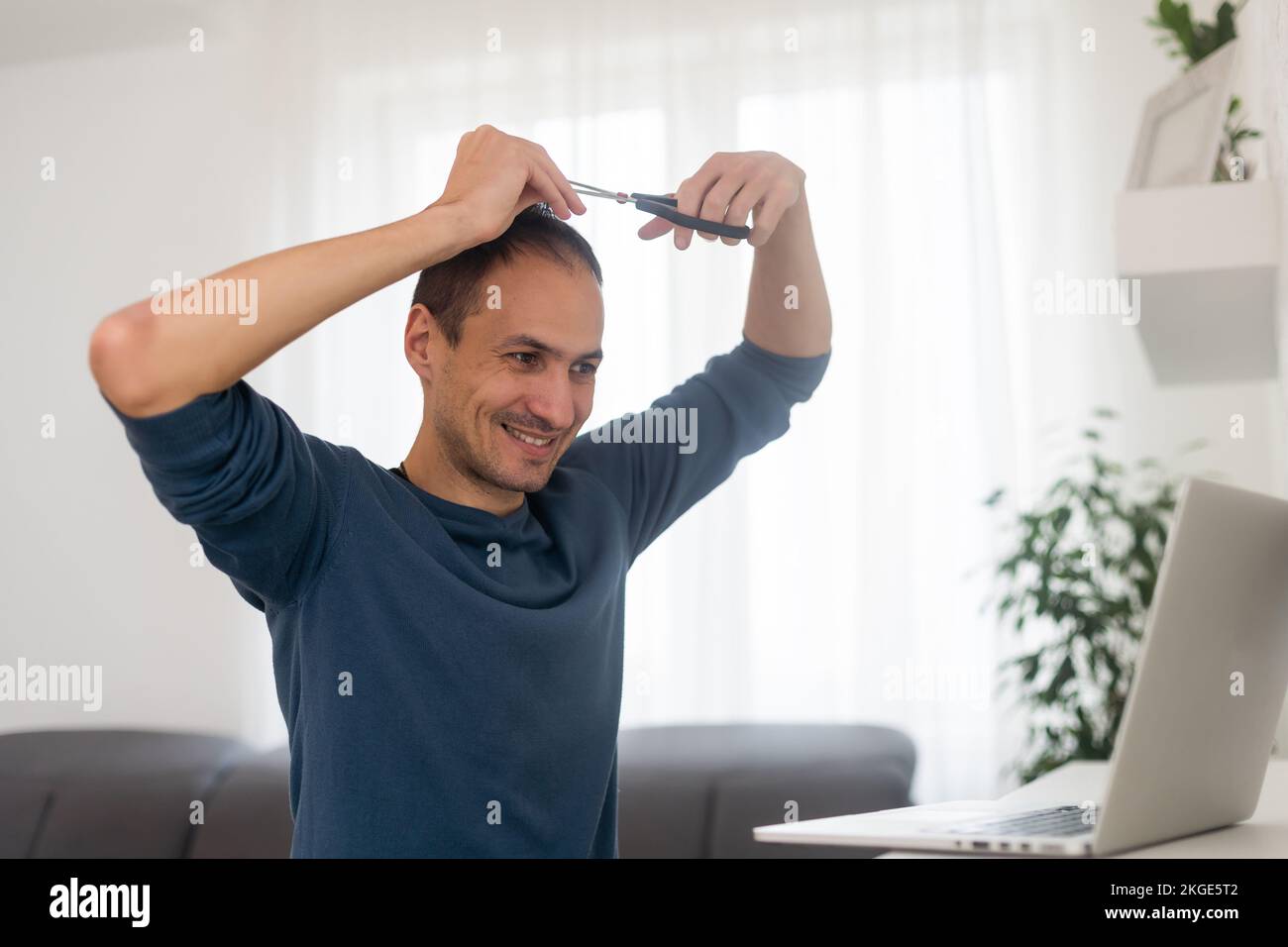 Shaggy man is trying to cut his own hair with the help of scissors and ...