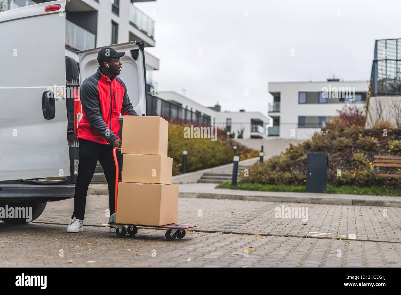 Black young adult delivery guy in work uniform unloading cardboard box ...