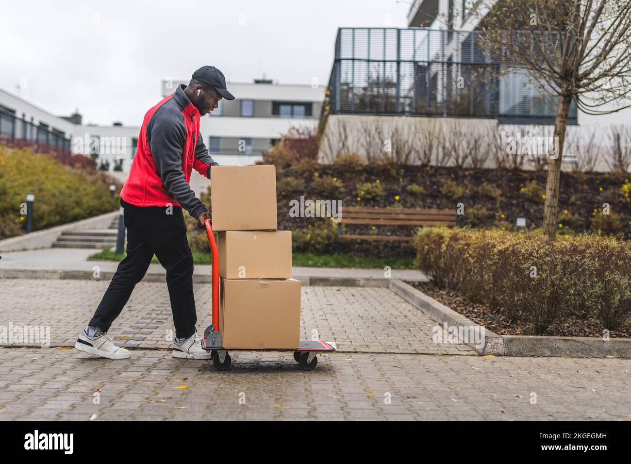 Black young adult delivery guy wearing work uniform walking on sidewalk ...