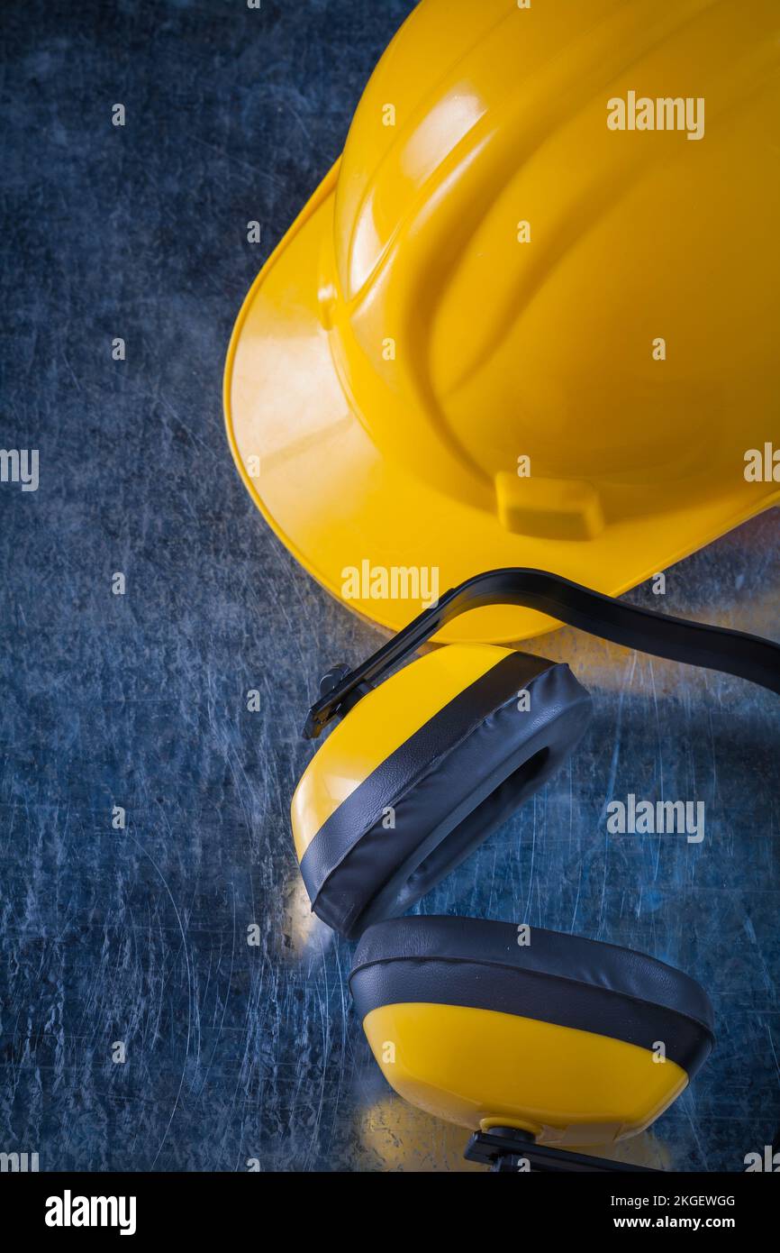 Protective yellow ear muffs and hard hat on scratched metallic ...
