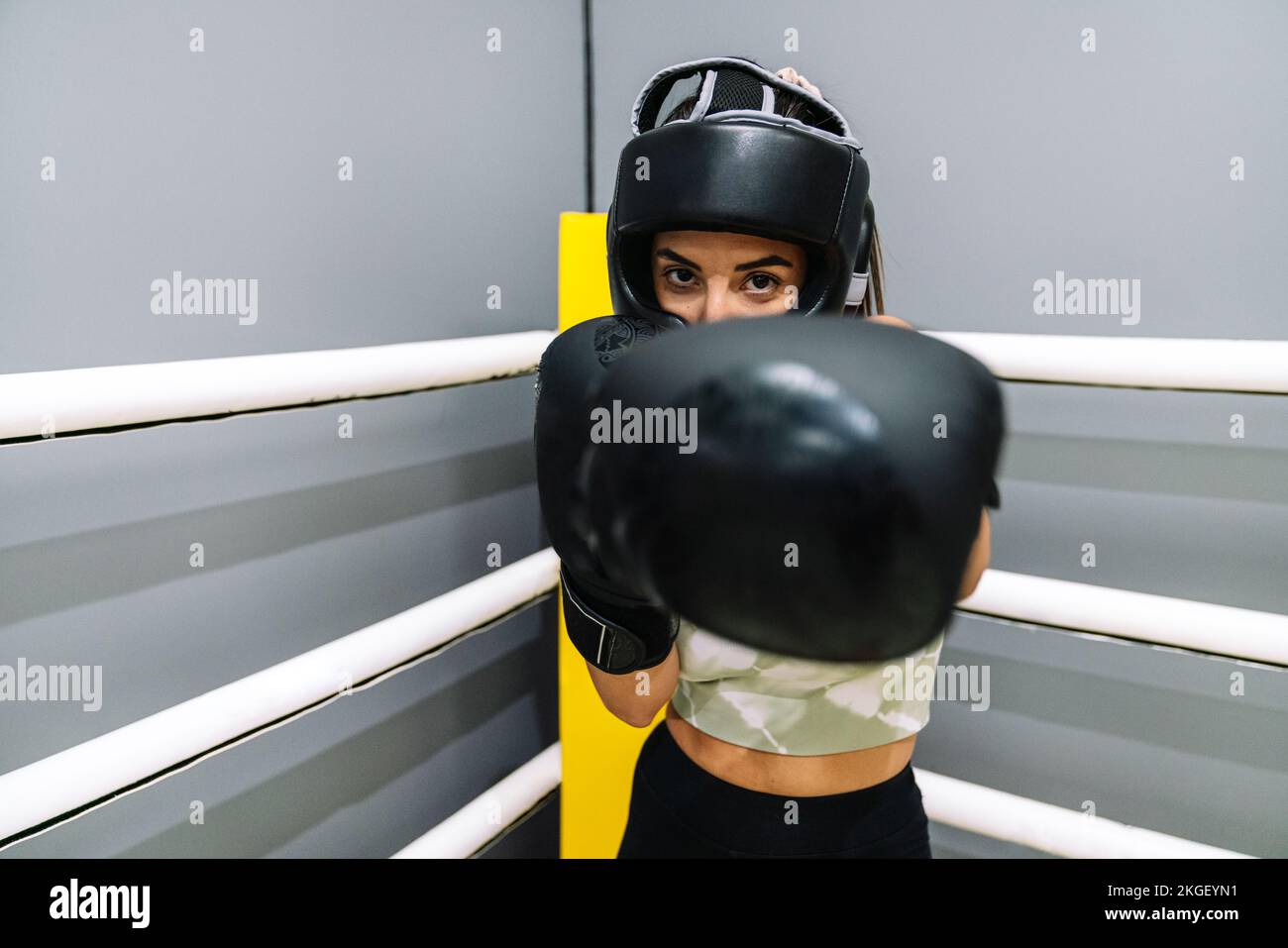 A young woman with boxing gloves and protective helmet throwing a punch ...