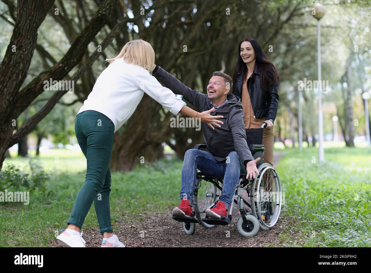 Women friends walking with disabled man in wheelchair in park, happy to ...