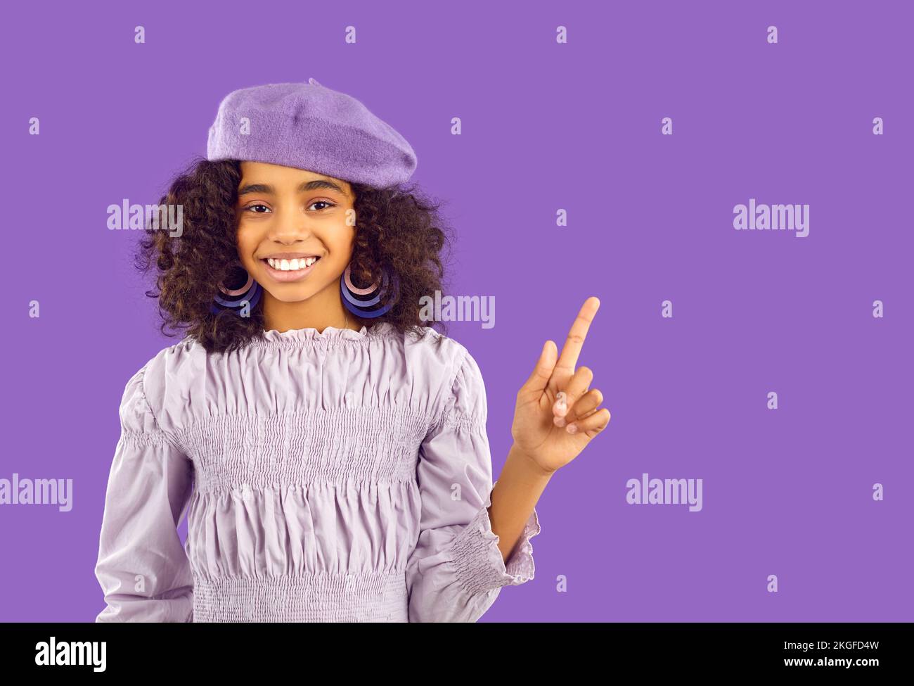 Pretty African girl in trendy beret hat pointing finger at copy space ...