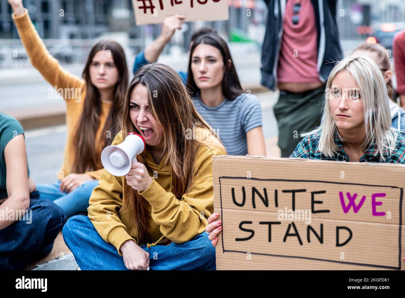 Young female protester giving a slogan using megaphone with group of ...
