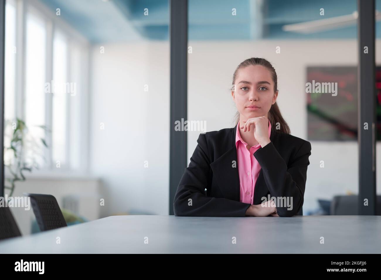 Successful young female leader in a suit with a pink shirt sitting in a ...