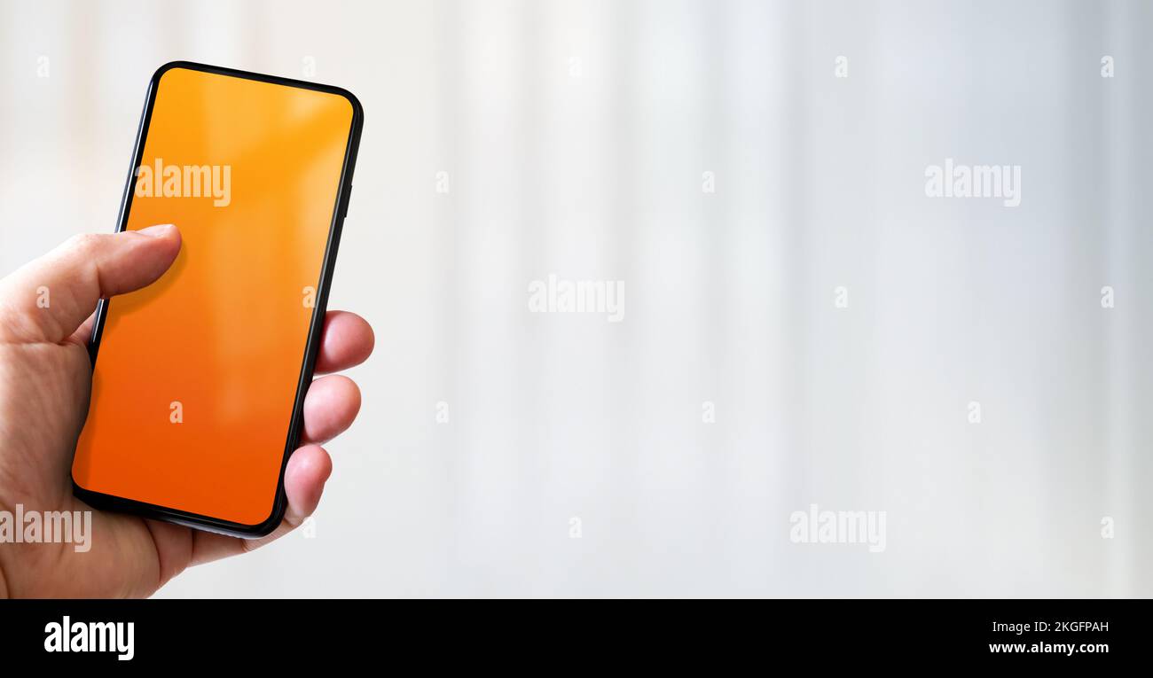 Hand holding a smartphone with blank orange screen. White office ...