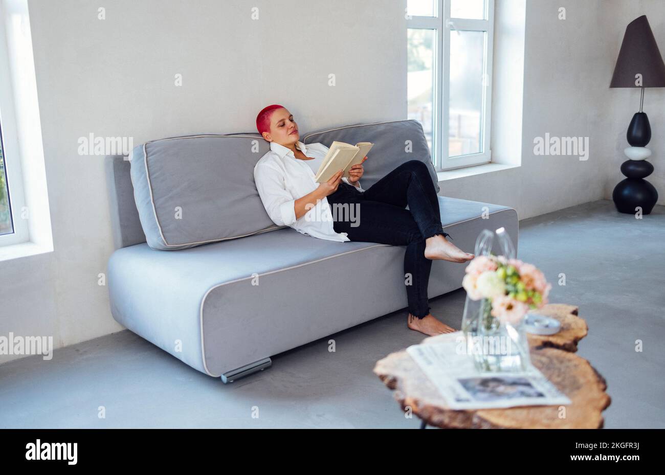 Young redhaired bald woman smiles and reads a novel at home on the ...