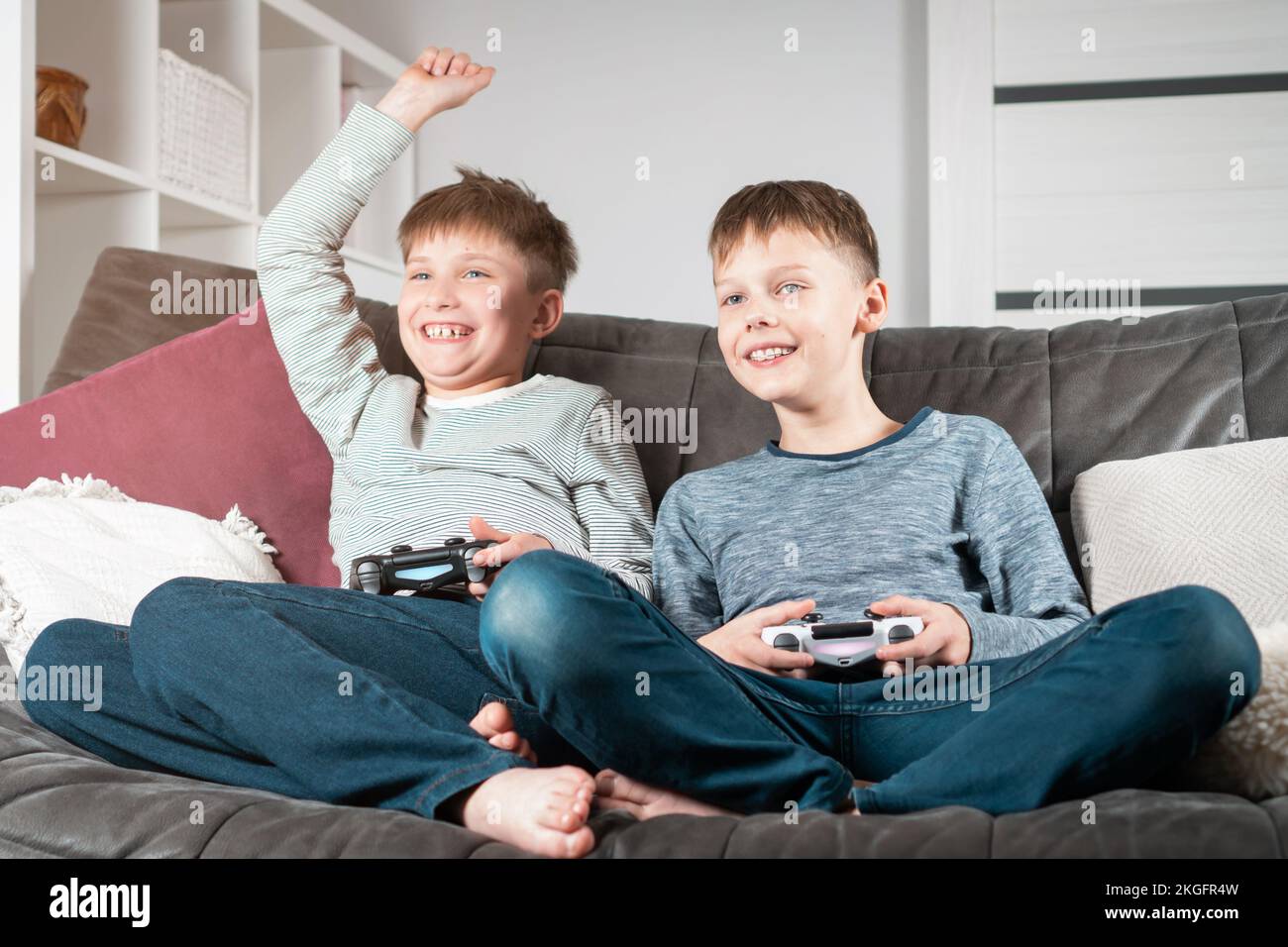 Portrait of two smiling pleased teenage boys children sitting on sofa ...