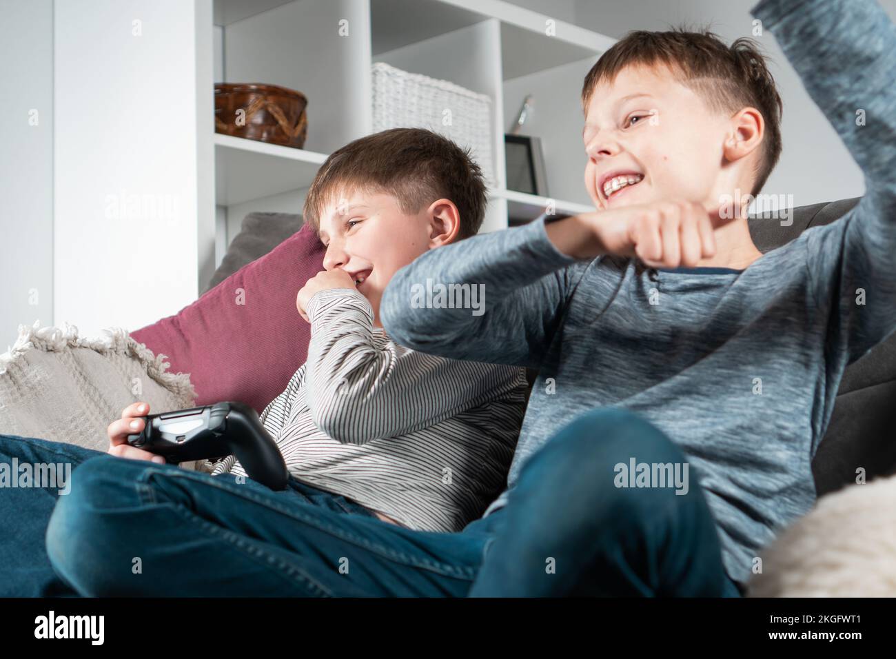 Portrait of two laughing teenage boys children sitting on grey sofa at ...
