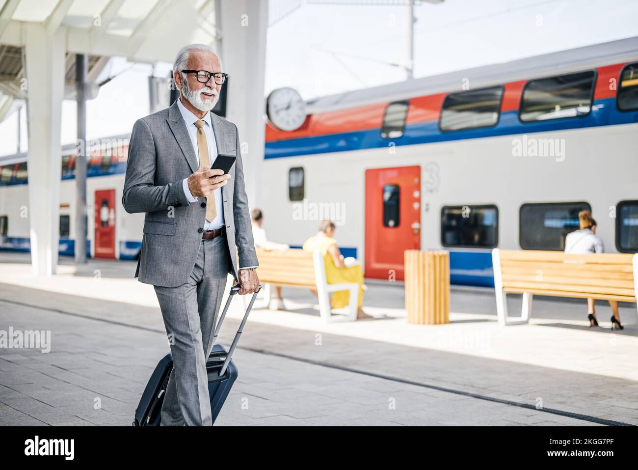 Smiling entrepreneur holding smart phone while walking with suitcase ...