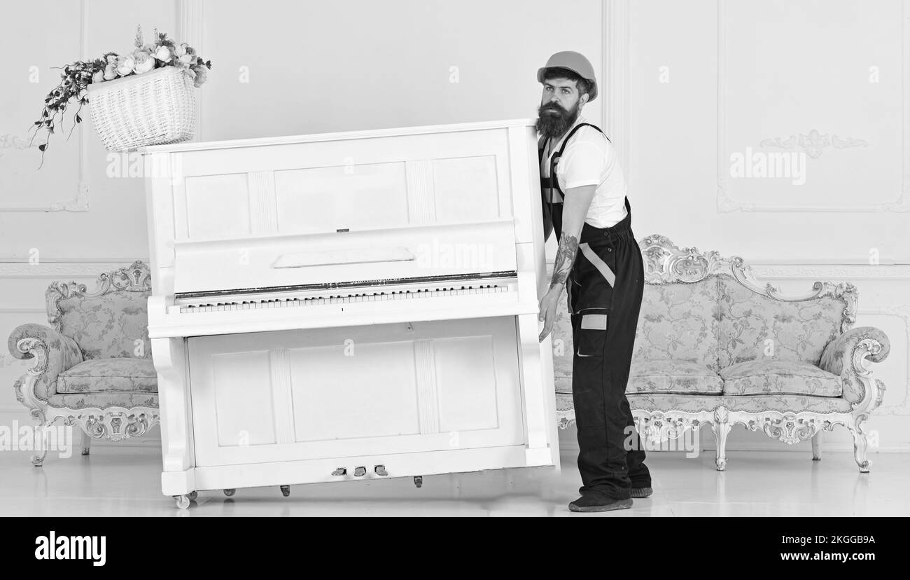 Loader moves piano instrument. Man with beard worker in helmet and ...