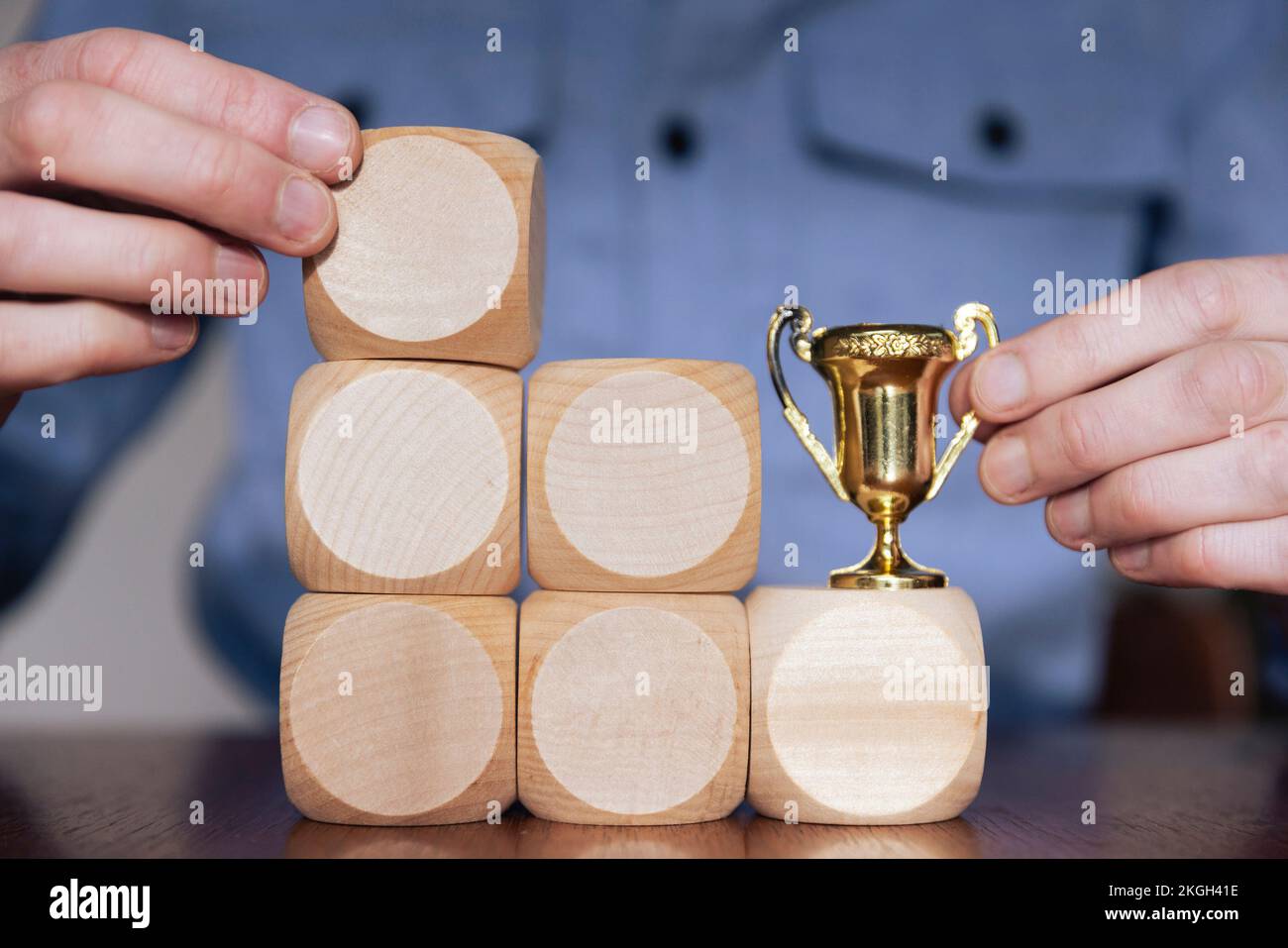 Business person arranging large wooden blocks with a winning trophy ...
