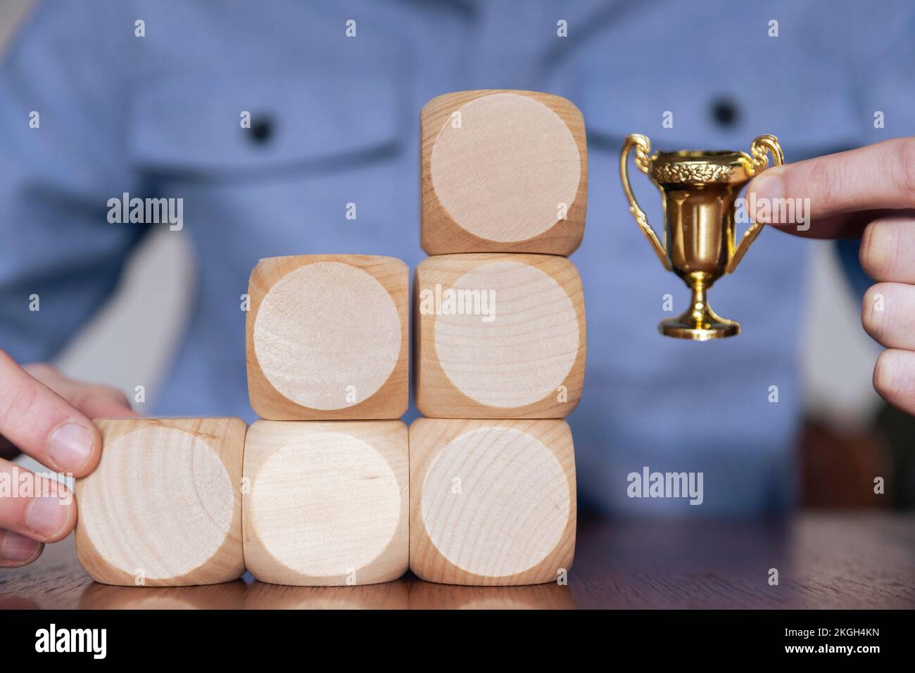Business person arranging large wooden blocks with a winning trophy ...