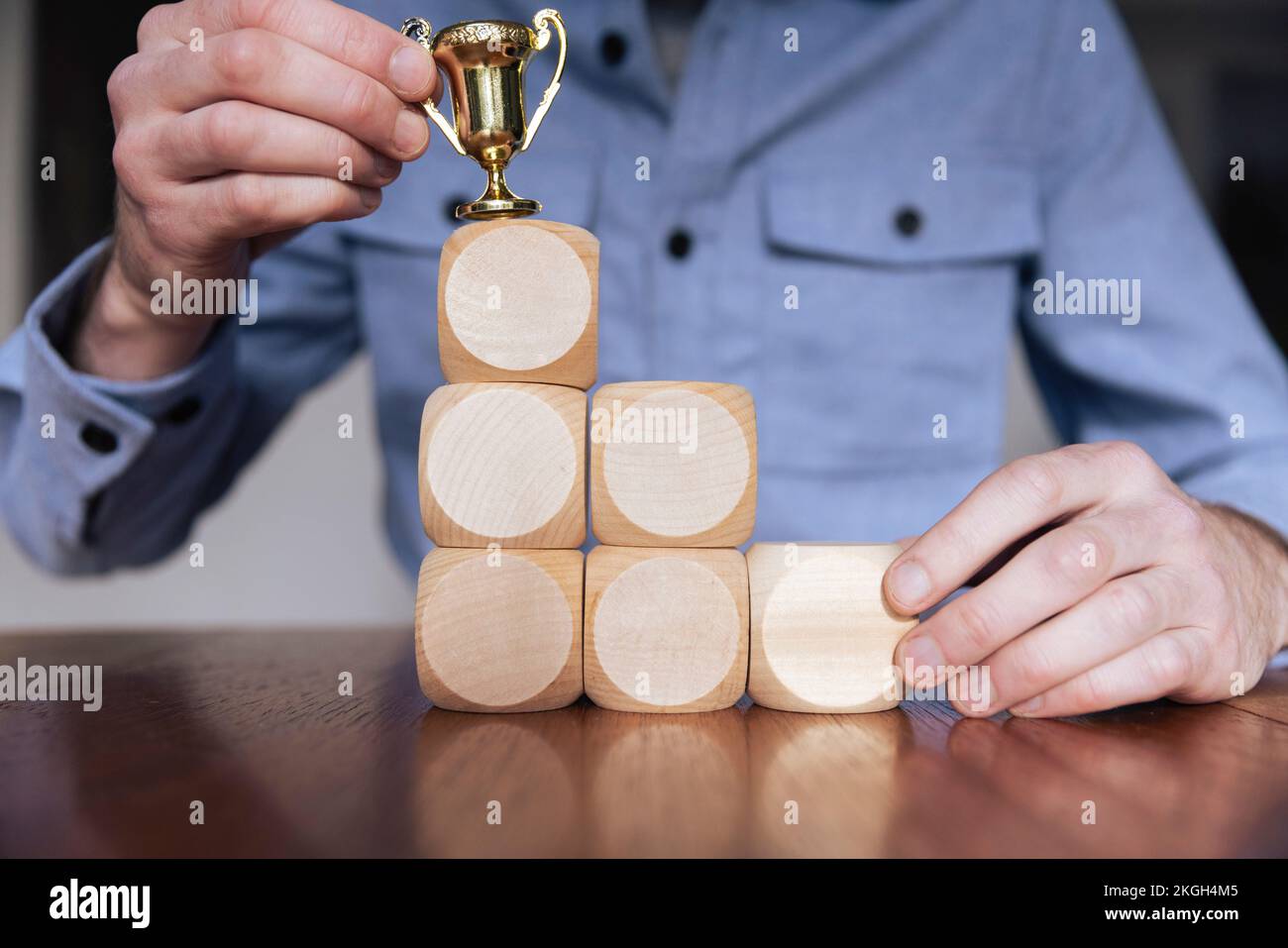 Business person arranging large wooden blocks with a winning trophy ...