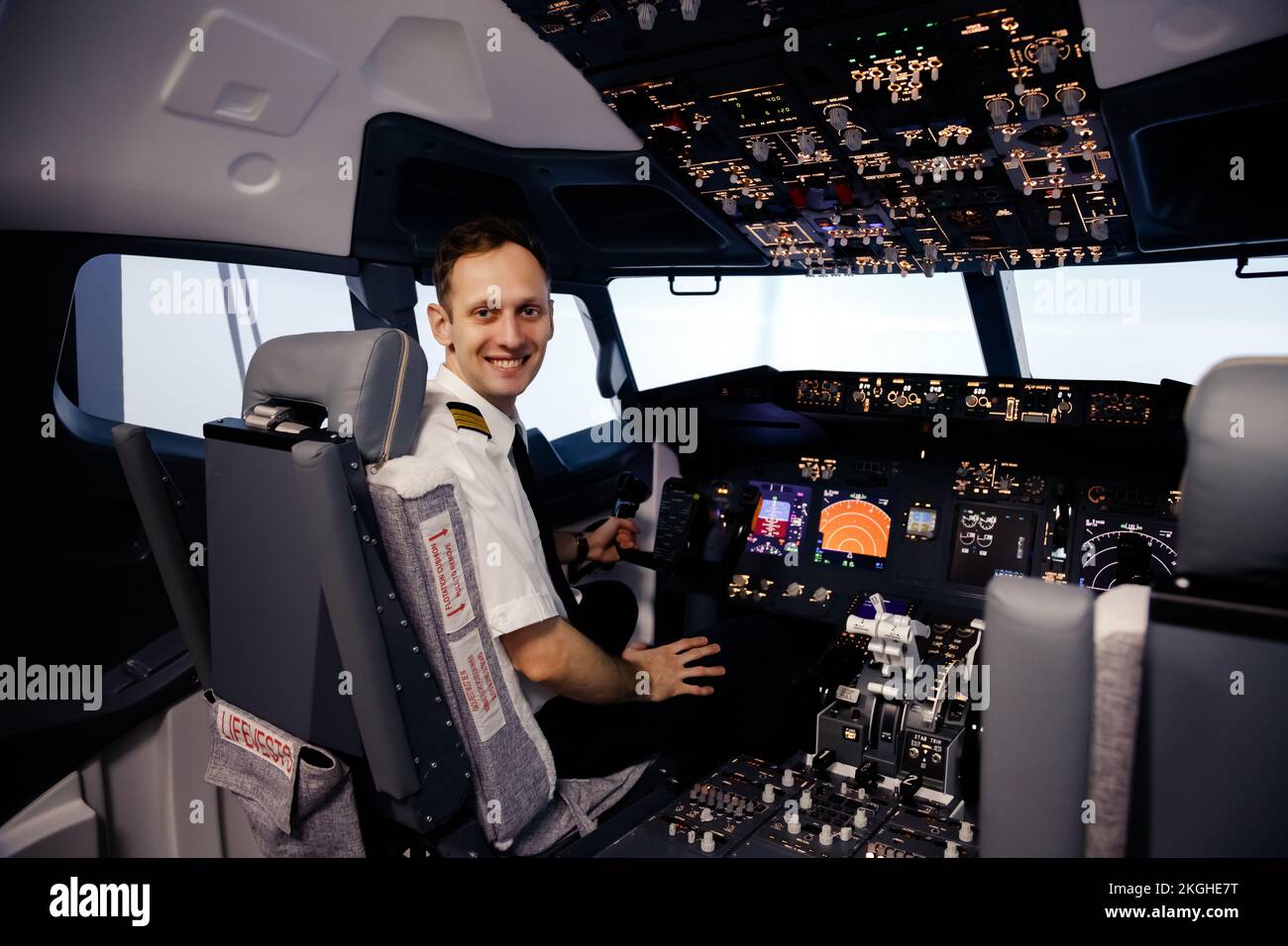 Pilot in cockpit. Rear view of confident male pilot looking over shoulder and smiling while ...