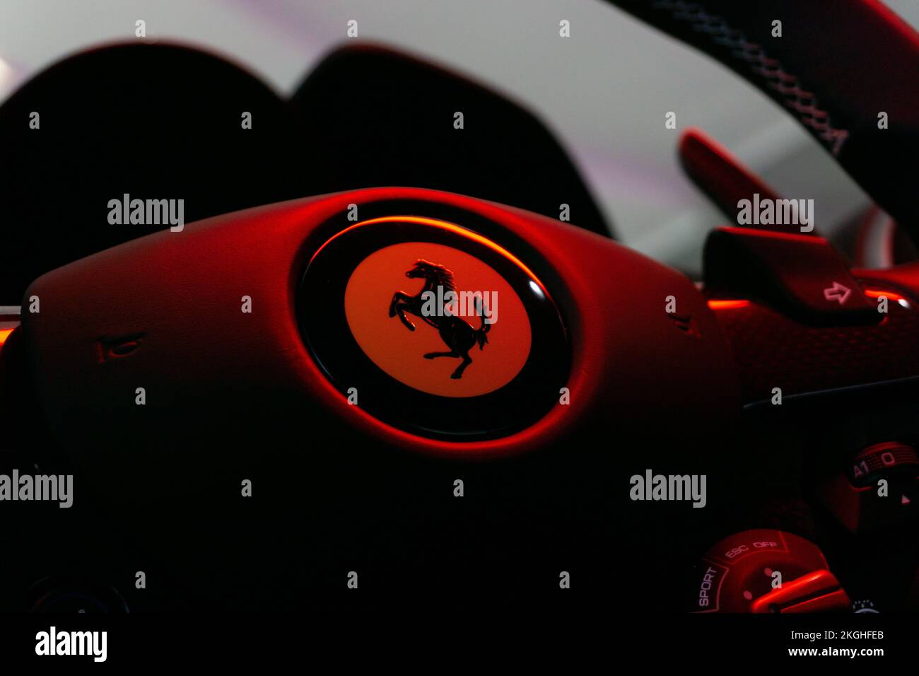 A closeup shot of a steering wheel of a Ferrari car under red lights ...