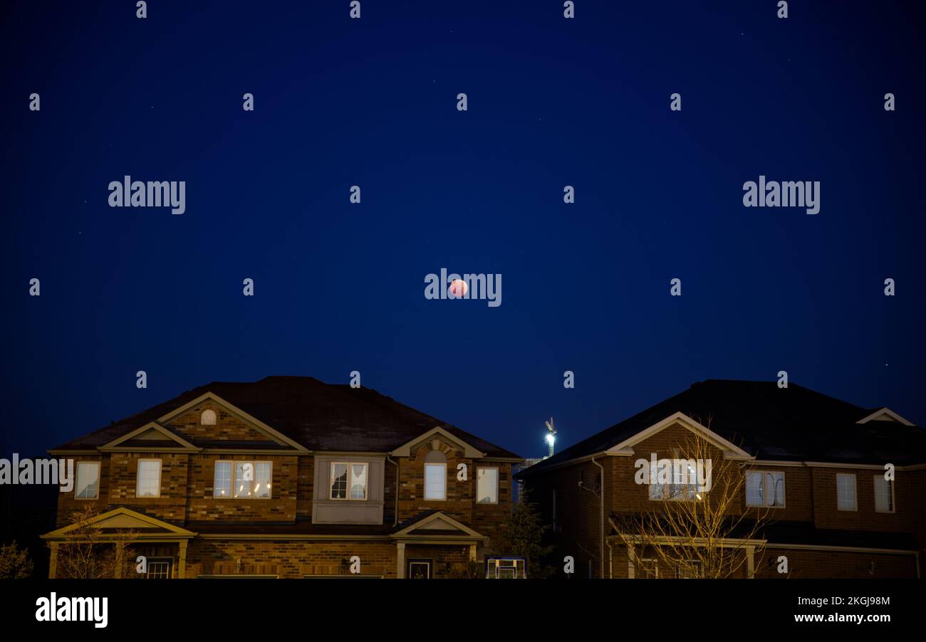 A low-angle of houses near road with street lights lunar eclipse on the ...
