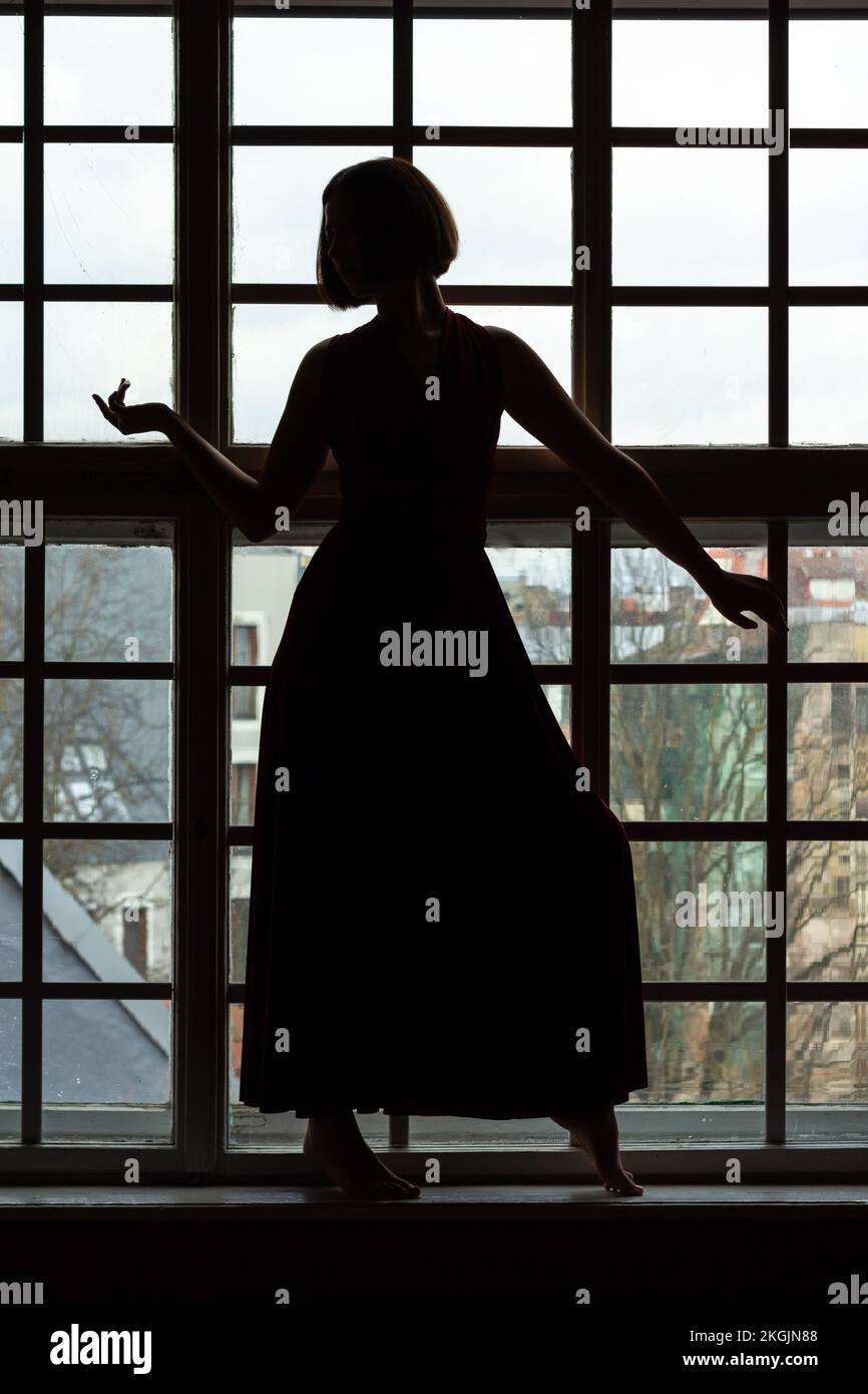 Silhouette of a woman in a red dress with head turned in front of a ...