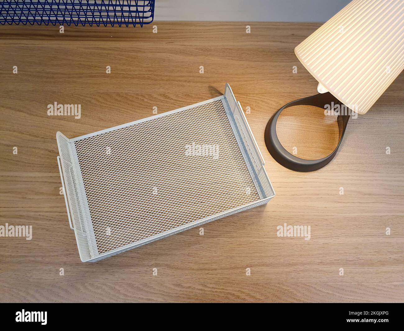 Empty mesh metal paper tray and table lamp on table. Workplace concept ...