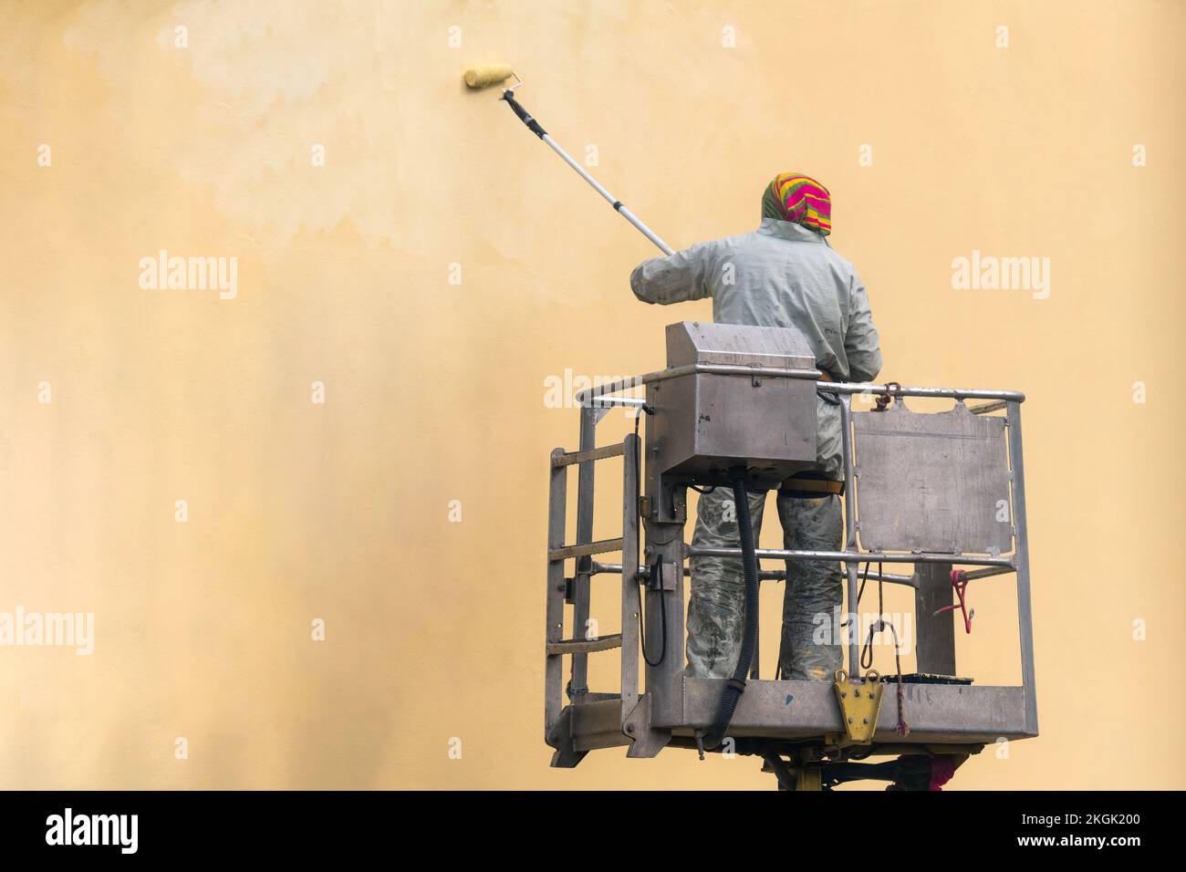 Man on a lifting platform painting the building wall with a roller ...