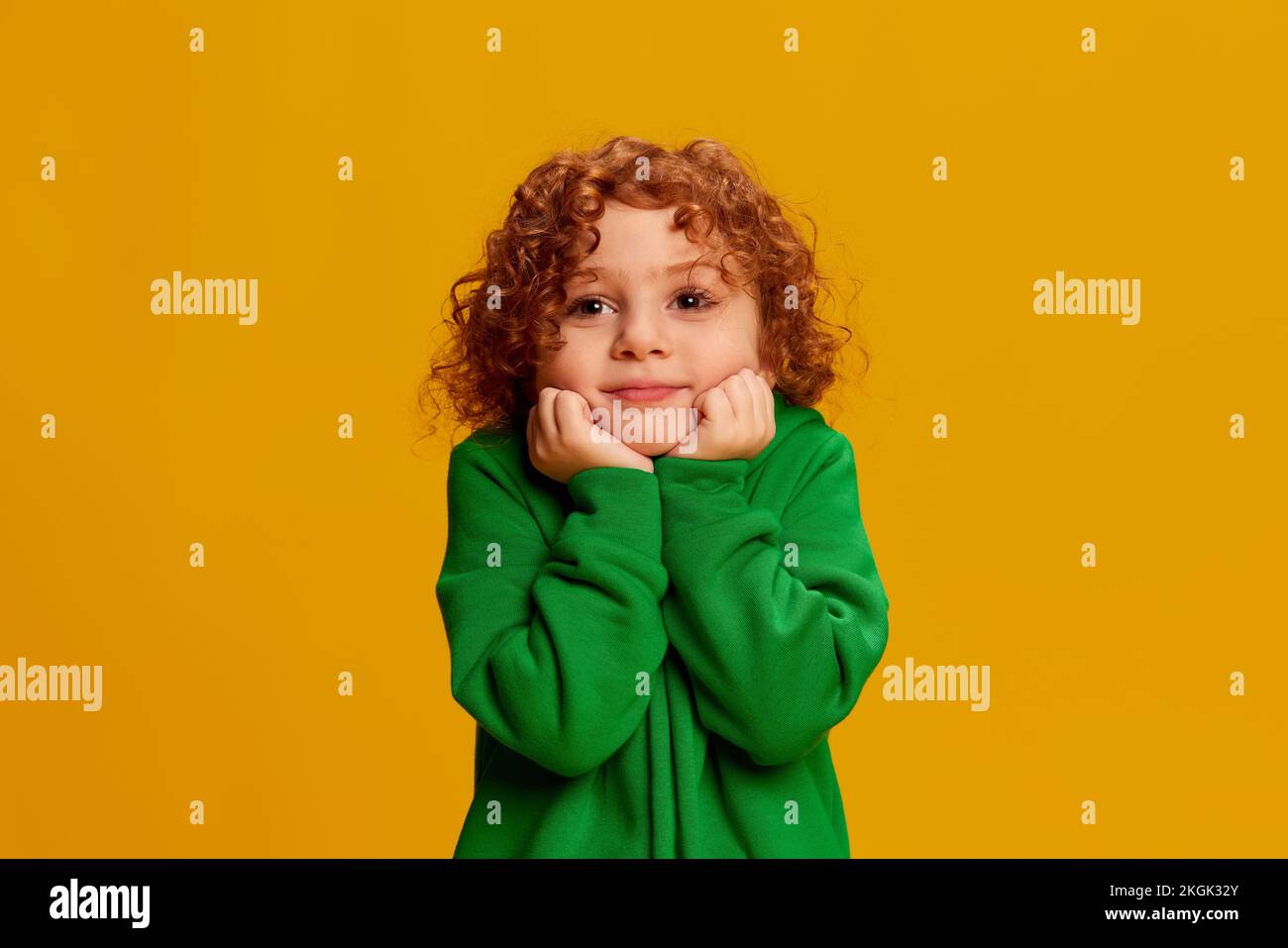 Portrait of cute little girl, child with curly red hair posing isolated over yellow background ...
