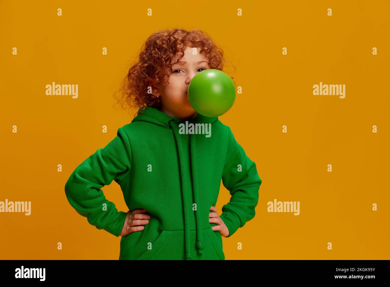 Portrait of cute little girl, child with curly red hair posing with big bubble gum isolated over ...