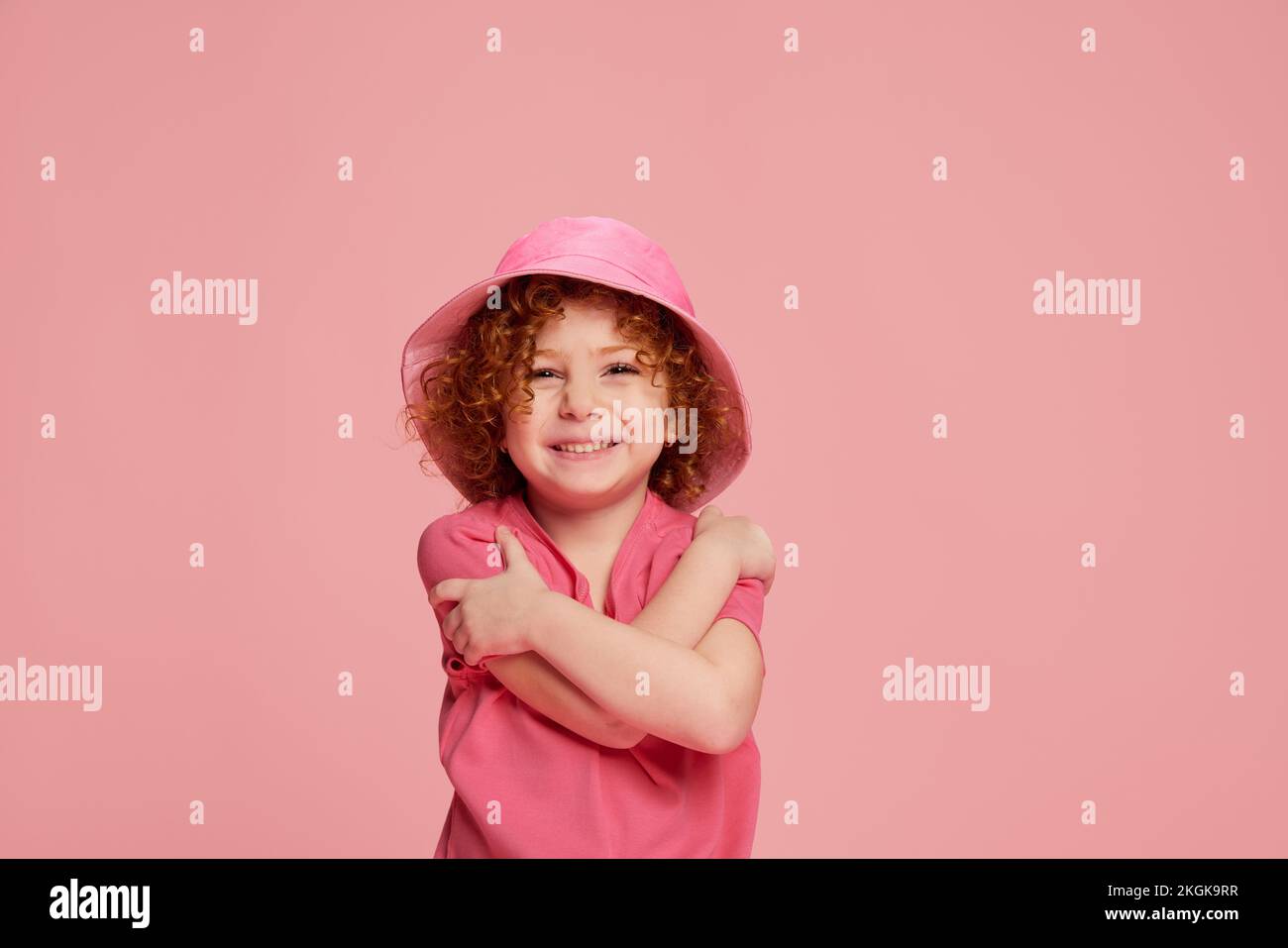 Portrait of cute little girl, child with curly red hair posing in panama and smiling isolated ...