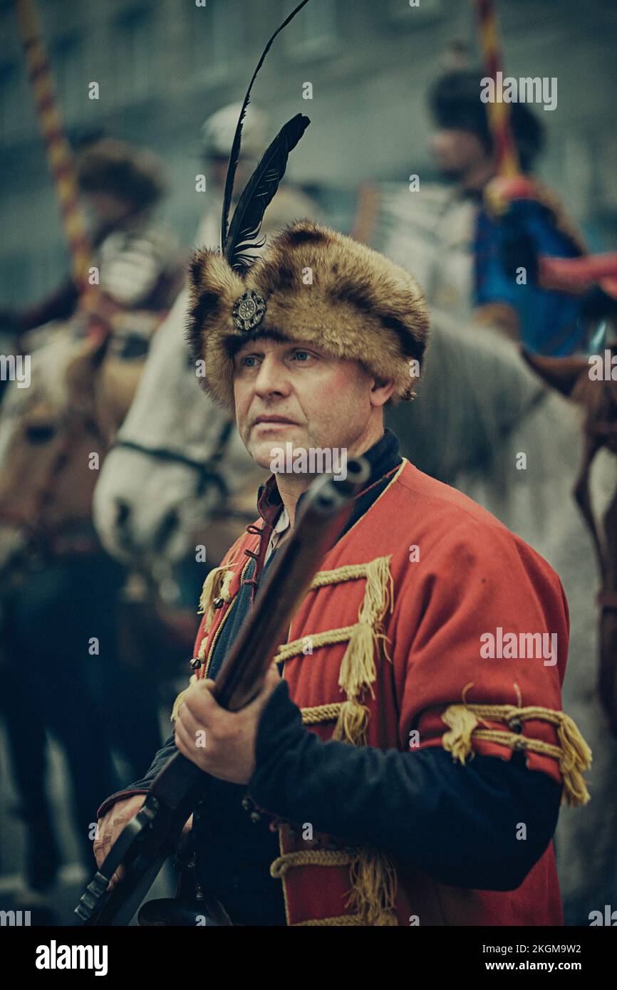 A vertical of a man in traditional Polish clothes holding a riffle on ...