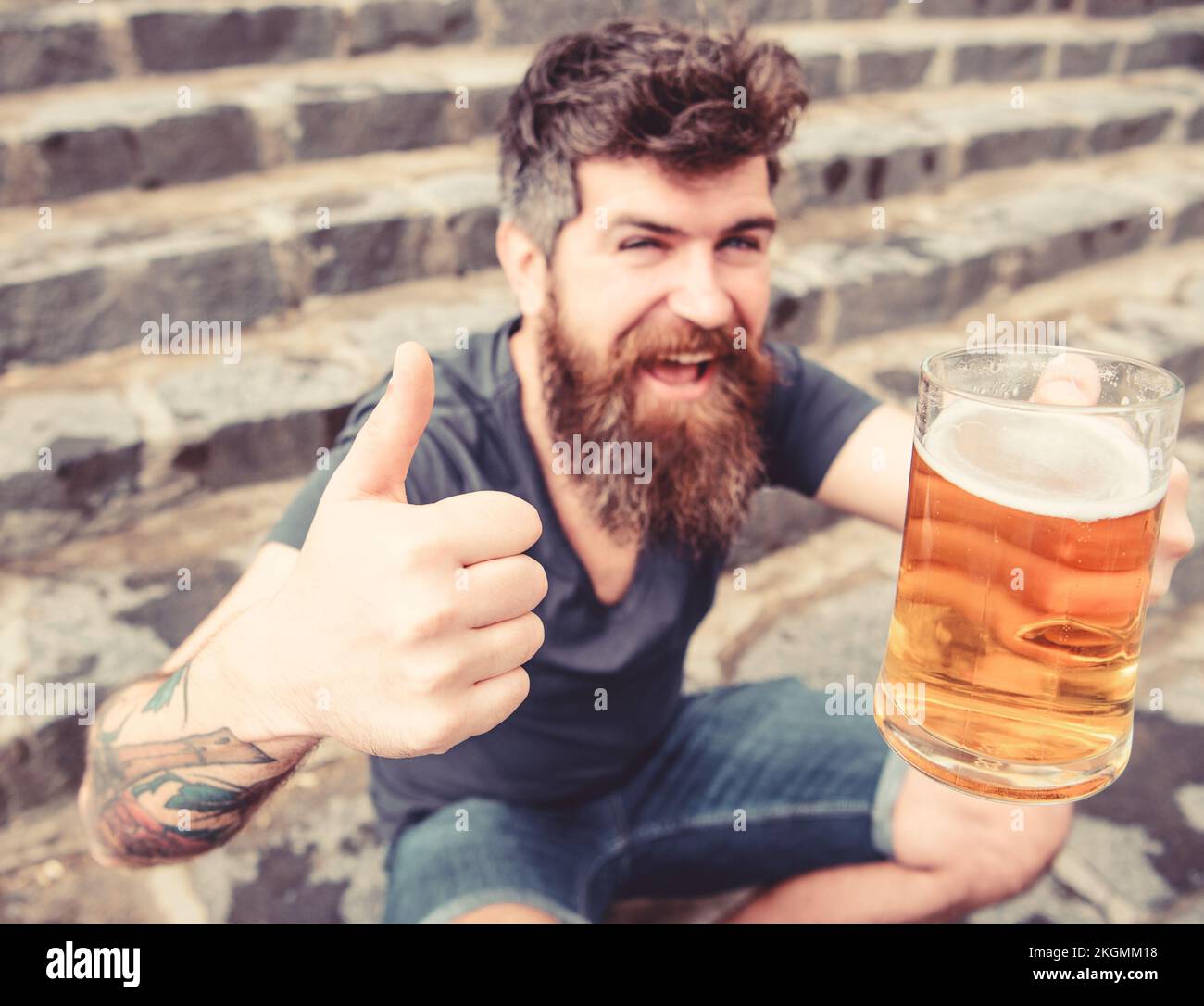 Man with beard and mustache holds glass with beer and shows thumb up ...
