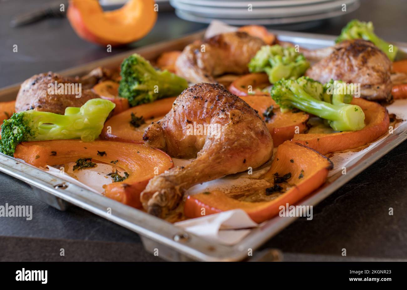 Crispy baked chicken legs with red kuri squash and broccoli on a baking ...