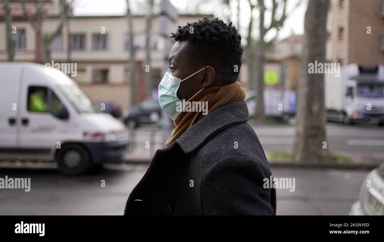 Young black man wearing covid-19 face mask walking in city downtown ...
