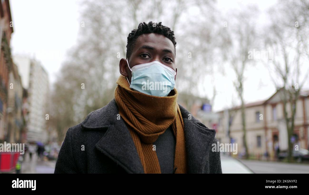 Young black man wearing covid-19 face mask while walking in city ...