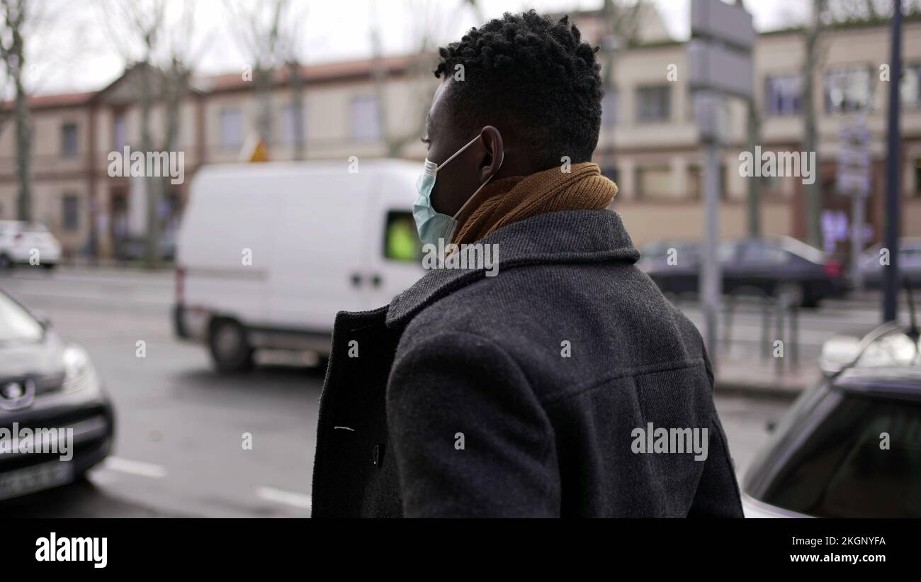 Young black man wearing covid-19 face mask walking in city downtown ...