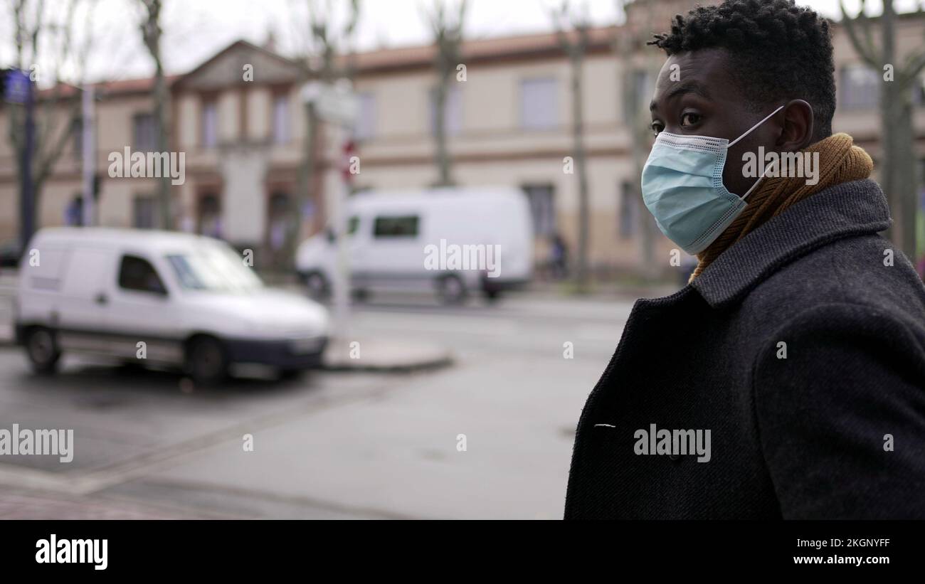 Young black man wearing covid-19 face mask walking in city downtown ...