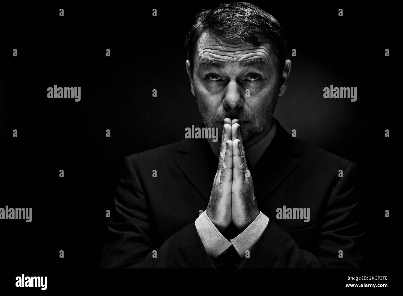 Mature man in full suit praying against black background, close up ...