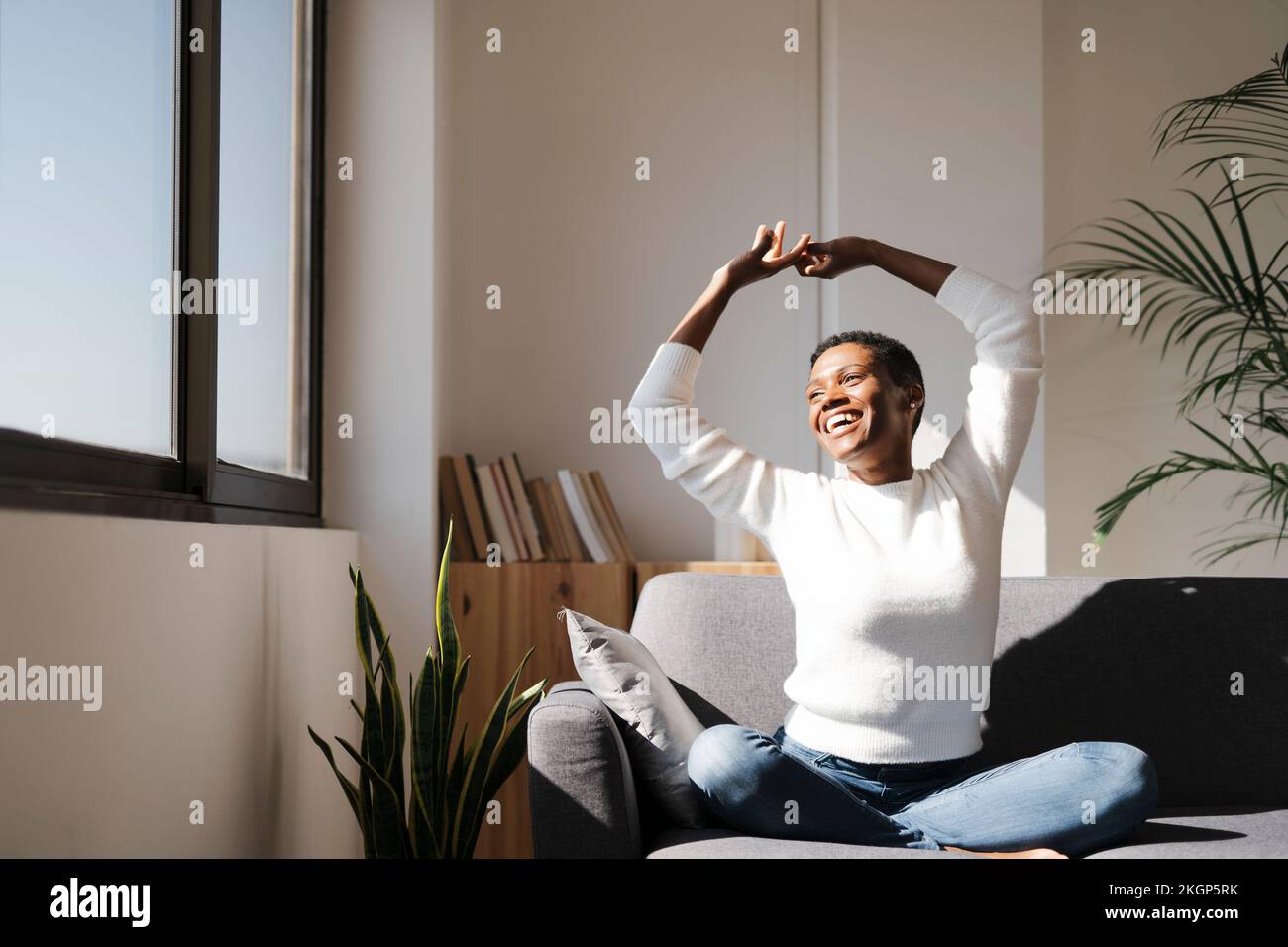 Laughing woman sitting on couch at home stretching her arms Stock Photo ...