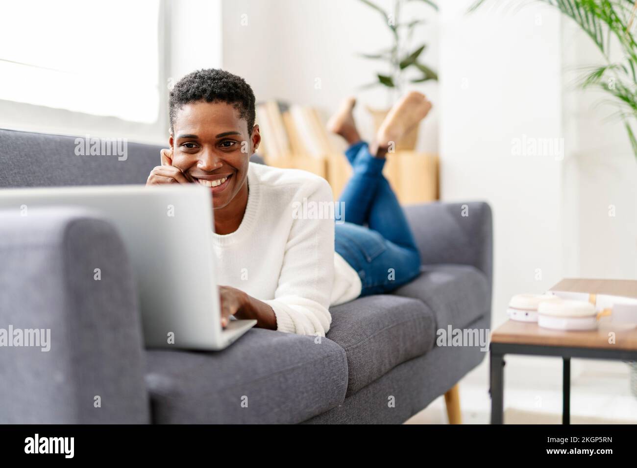 Smiling woman lying on couch using laptop Stock Photo - Alamy
