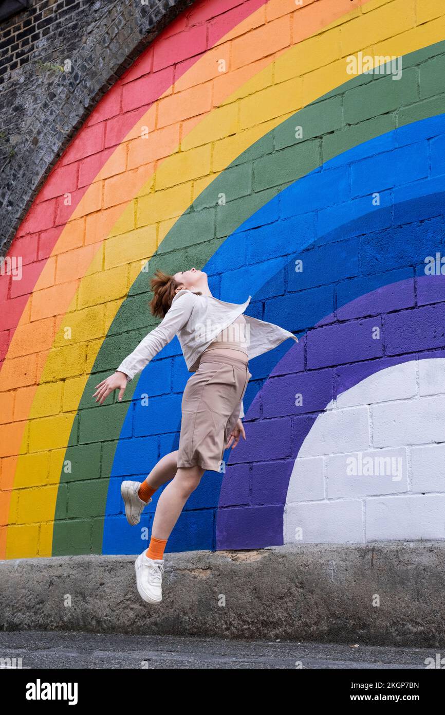 Young woman jumping in front of rainbow colored wall Stock Photo - Alamy
