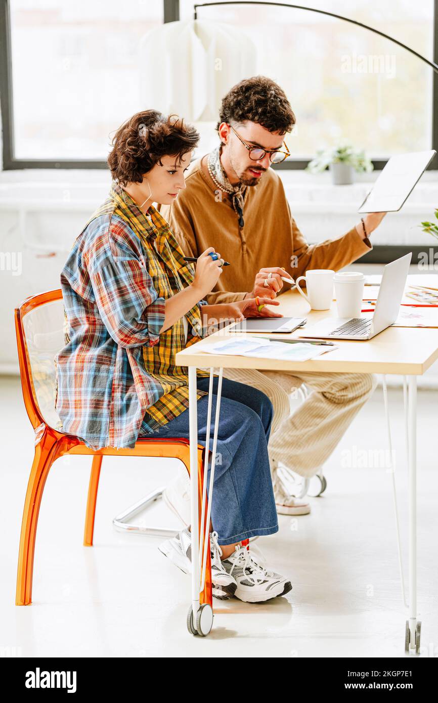 Illustrator with colleague working on laptop at desk Stock Photo - Alamy