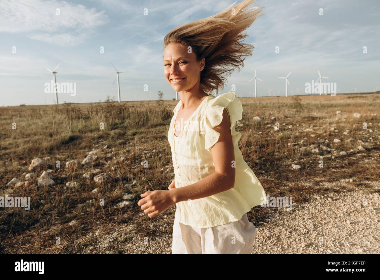 Happy woman running in front of wind turbines at field Stock Photo - Alamy
