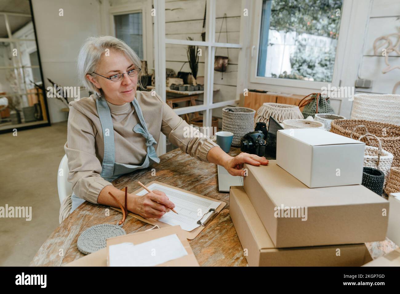 Mature craftswoman with clipboard analyzing box on workbench Stock ...