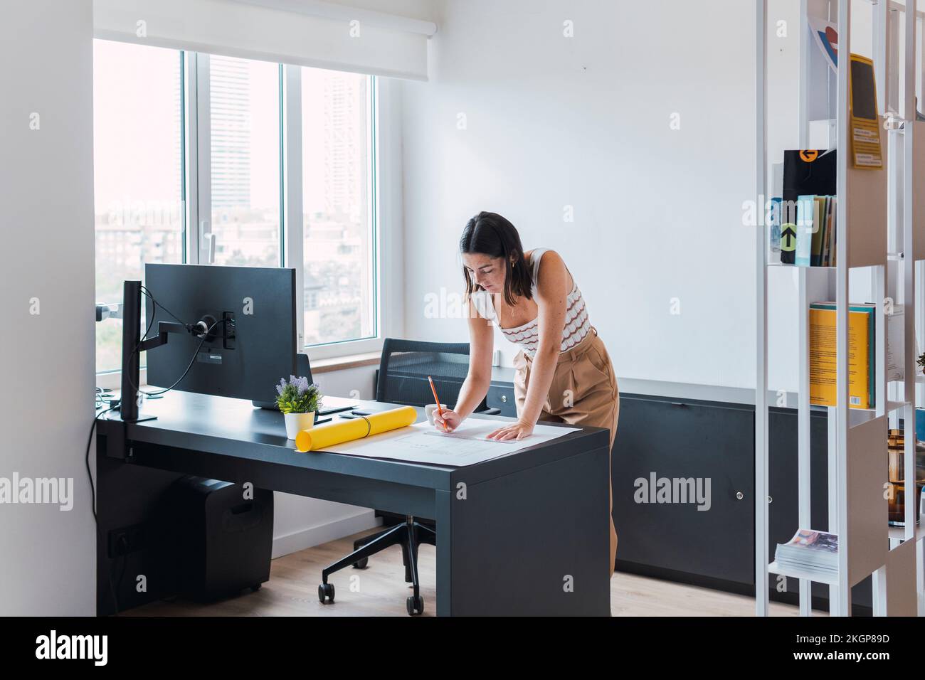 Young architect leaning on desk analyzing blueprint in office Stock ...