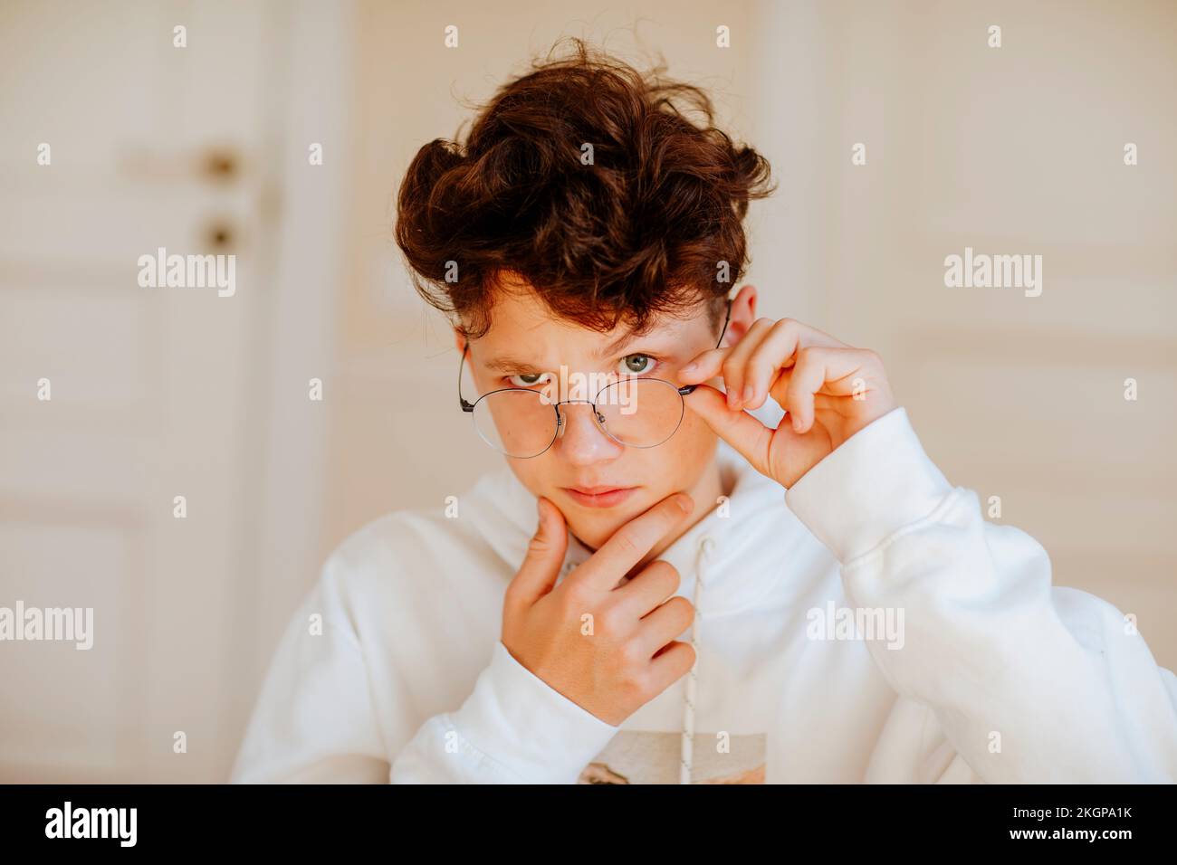 Boy adjusting eyeglasses with hand on chin at home Stock Photo - Alamy