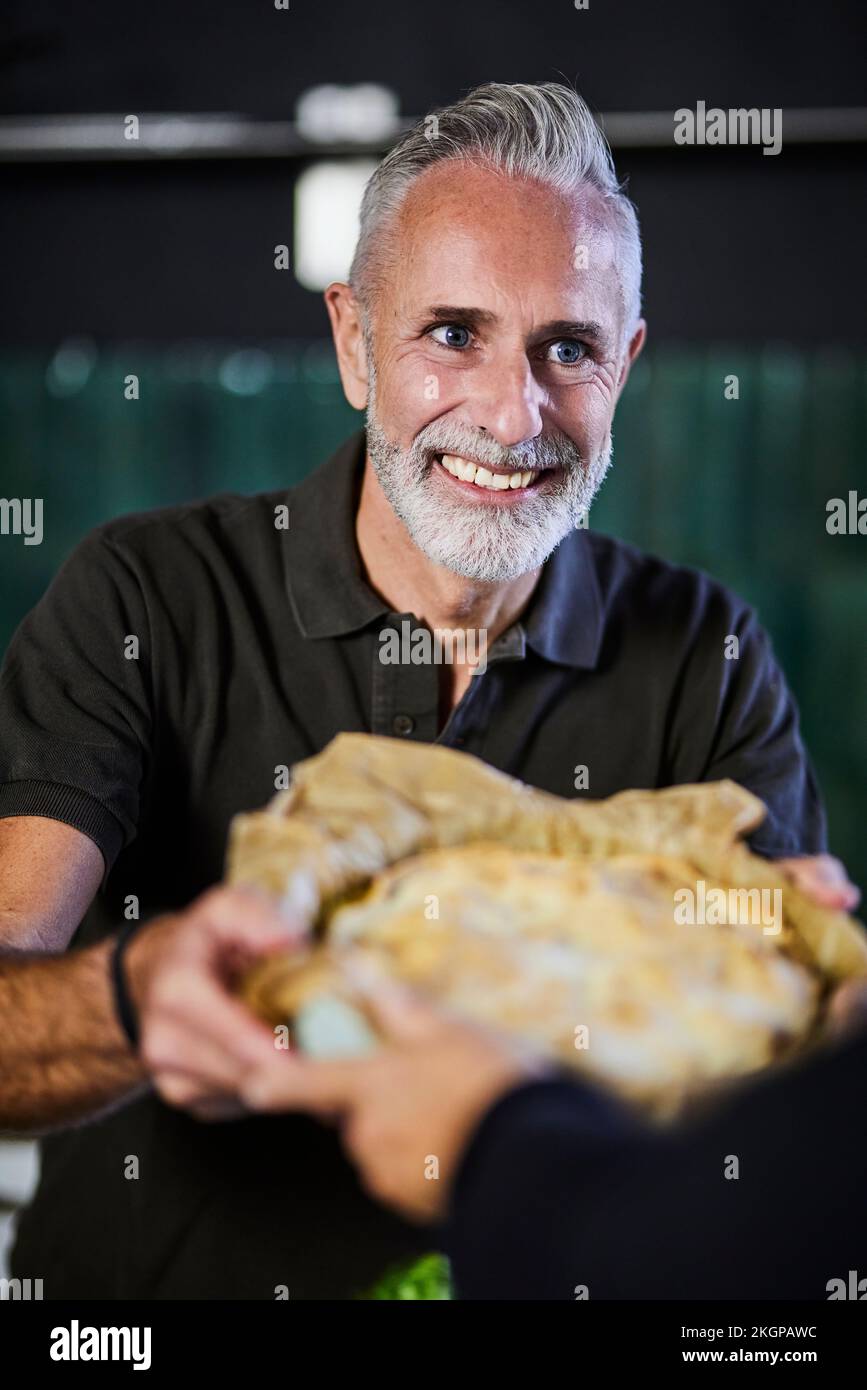 Happy mature man handing over savory pie Stock Photo - Alamy