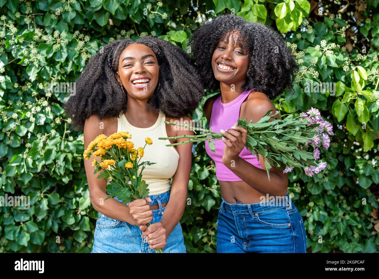 Happy friends holding flowers in front of plant Stock Photo - Alamy